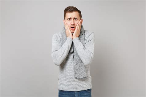 회색 스웨터 스튜디오에서 회색 벽 배경에 고립 된 뺨에 손을 퍼 팅 스카프에 충격 젊은 남자 건강 한 패션 라이프 스타일 사람들