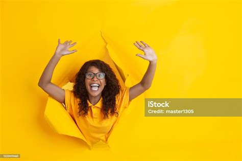쾌활한 젊은 여성은 찢어진 노란색 종이 구멍 배경 감정과 표현에서 포즈 구멍에 대한 스톡 사진 및 기타 이미지 구멍 한 명의 여자만 명랑한 Istock