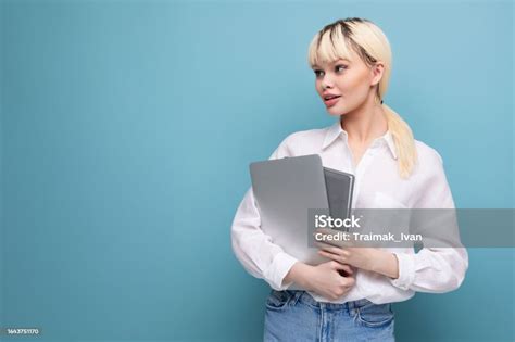 흰 셔츠와 청바지를 입은 짧은 머리를 한 젊은 금발의 백인 여성은 복사 공간을 배경으로 업무용 노트북과 노트북을 들고 있다 사업 이념 20 24세에 대한 스톡 사진 및 기타