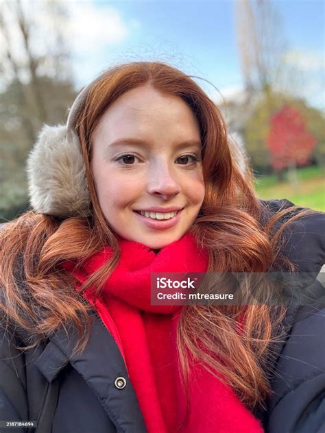 검은 패딩 재킷 빨간 스카프와 인조 모피 귀마개를 입고 매력적인 빨간 머리 여자의 클로즈업 이미지 카메라를보고 얼굴 사진 인물 사진 야외 공공 공원 설정 전경에 초점 20