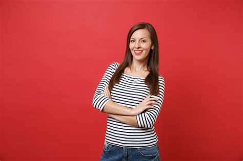 캐주얼 스트라이프 옷 서 고 접혀 손을 잡고 밝은 빨간 벽 배경에 고립에서 아름 다운 젊은 여자의 초상화 사람들이 진심으 감정 라이프 스타일 개념 복사 공간을 비웃는 다