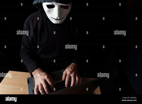 Hacker Man Dressed In Black Hooded With Mask Typing On A Computer Cybercrime Concept Stock