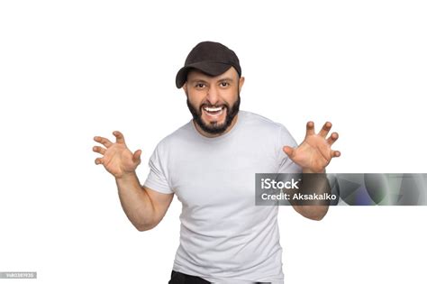 하얀 티셔츠를 입고 모자를 쓴 젊은 수염 난 남자의 초상화는 카메라를 보고 있다 발톱처럼 손으로 포즈를 취하는 남자 흰색 배경에 격리된 스튜디오 촬영 30 34세에 대한