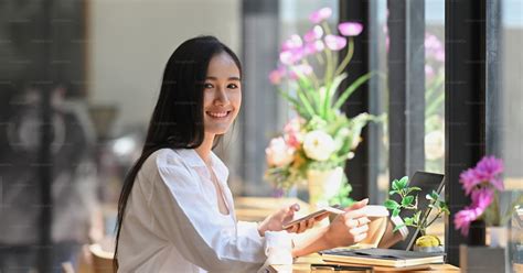 흰색 셔츠를 입은 멋진 여성의 사진이 스타일러스 펜과 컴퓨터 태블릿으로 작업하면서 현대적인 카페레스토랑 위의 나무 카운터 바에 배경으로 앉아 있습니다 사진