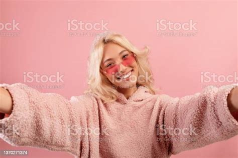행복한 블로거 여성이 셀카를 만들고 화려한 안경과 후드를 입고 포즈를 취하고 카메라 핑크 배경에 미소를 지었습니다 20 29세에 대한 스톡 사진 및 기타 이미지 Istock