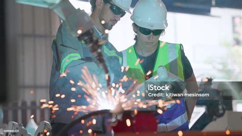 안전 유니폼을 입은 남녀 엔지니어 제어판을 사용하여 중공업 제조 공장의 용접 공작물에 로봇 팔을 제어합니다 기술자 팀이 공장에서 용접 화재 스파크 중 자동화 로봇 시스템