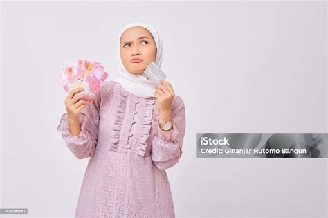 히잡과 보라색 드레스를 입고 흰색 스튜디오 배경에 격리된 신용 카드와 돈 지폐를 들고 있는 잠겨 있는 젊은 아시아 무슬림 여성 Eid Ul Fitr에 대한 스톡 사진 및