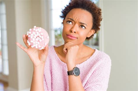 분홍색 설탕 마쉬 멜 로우를 먹는 젊은 아프리카계 미국인 여자 질문에 대해 생각 하는 도넛 심각한 얼굴 매우 혼란 스러운 아이디어 가정 생활에 대한 스톡 사진 및 기타