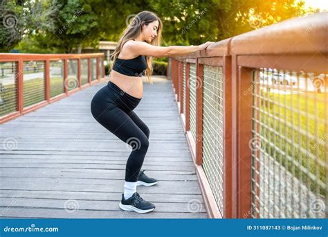 Full Length Side View Of Sporty Pregnant Woman Doing Squats Over Fence