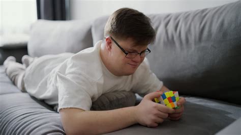 Premium Stock Video Down Syndrome Man Resting On The Couch At Home And Playing With Rubik Cube
