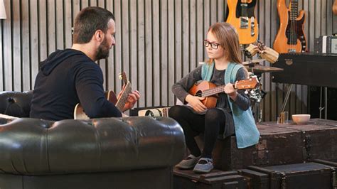 아빠는 딸에게 기타와 우쿨렐레를 가르치셨다 집에서 기타를 배우는 어린 소녀 측면 뷰 집에서 우쿨렐레 수업 그녀의 아버지로부터 기타를 배우는 아이 2명에 대한 스톡 사진 및