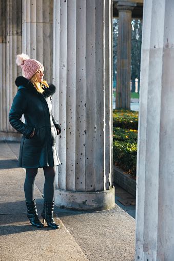 겨울 코트 재킷과 니트 모자를 쓴 중반 성인 여성이 건축 기둥 옆에 서 있다 금발 머리에 대한 스톡 사진 및 기타 이미지 금발 머리 한 명의 여자만 45 49세