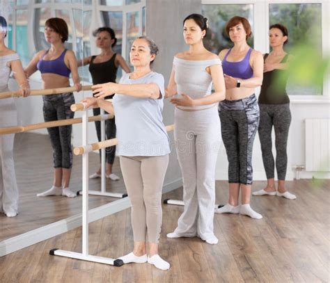 Elderly Woman Learning First Ballet Position At Barre In Group Class