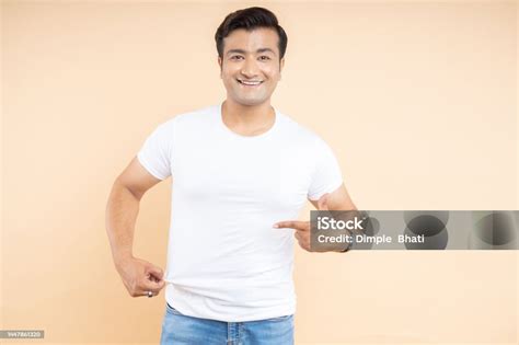 하얀 캐주얼 티셔츠를 입은 잘생긴 젊은 인도 남자가 빈 공간을 손가락으로 가리키고 있다 모형 디자인 인쇄의 정면도입니다