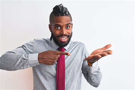 고립된 흰색 배경 위에 넥타이를 매고 서있는 아프리카 계 미국인 사업가는 손으로 손가락으로 가리키는 동안 카메라에 놀랍고 미소를