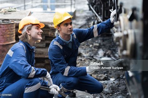 남성과 여성 엔지니어 유지 보수 기관차 엔진 기관차 수리 차고에서 안전 유니폼 헬멧 및 장갑을 착용 남성과 여성 철도 엔지니어는 차고에서 렌치 수리 기차 바퀴를 사용합니다
