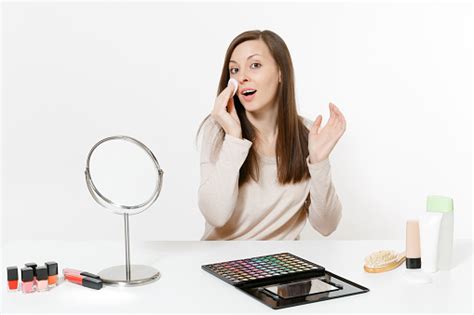 매력적인 재미 여자 얼굴 스폰지와 그녀의 피부 얼굴을 지워 버리고 흰색 바탕에 격리 설정된 얼굴 장식 화장품으로 메이크업을 적용 하는 테이블에 앉는 다 뷰티 여성 패션