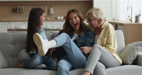 Multigenerational Women Tickling Each Other Laughing Seated On Sofa
