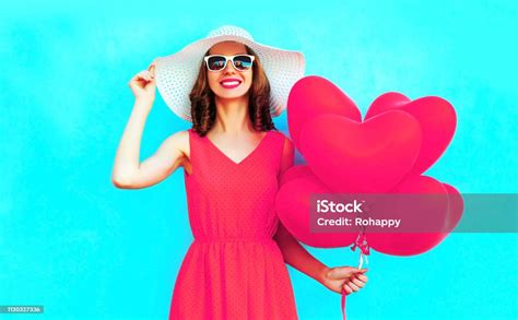 세로 행복 한 웃는 여자 여름 밀 짚 모자를 쓰고 파란색 배경에 분홍색 심장 모양 공기 풍선을 보유합니다 감정에 대한 스톡 사진