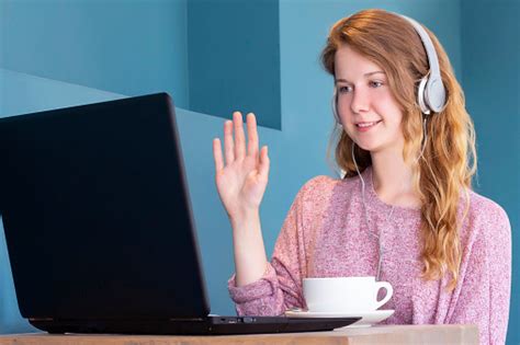 헤드폰을 착용 한 소녀가 노트북에서 화상 채팅을 통해 통신합니다 원격 작업 온라인 커피 한 잔과 함께 카페에있는 소녀 손을