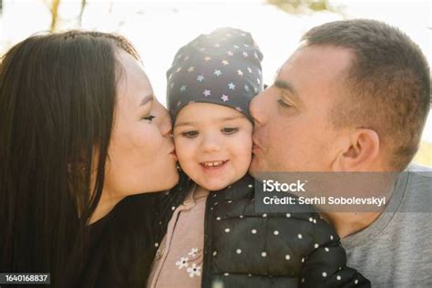 엄마와 아빠는 숲의 노란 나뭇잎을 배경으로 딸에게 키스하고 포옹한다 상반부 근접 촬영 젊은 가족은 해질녘에 함께 시간을 보낸다 가을 가족 사진 가을 공원에서 행복한 가족