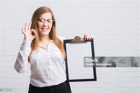 젊은 성인 비즈니스 여자 흰색 벽돌 벽 잡고 클립보드 손가락 우수한 기호 확인 표시를 하 고 서 개념에 대한 스톡 사진 및 기타 이미지 Istock
