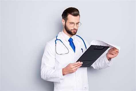 백색 실험실 외 투에 그의 목에 청진 기 집중된 바쁜 의사의 검사 회색 배경에 격리 분석 질병 역사 클립보드 확인 Expertising 들고 건강 진단에 대한 스톡 사진 및