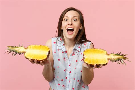 여름 옷을 입고 입을 열고 분홍색 파스텔 배경에 고립 된 신선한 파인애플 과일의 Halfs를 유지 하는 젊은 여자를 깜짝 놀라게 사람들은 생생한 라이프 스타일 휴식 휴가