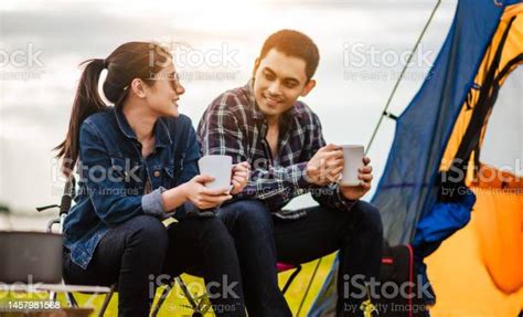 행복한 아시아 젊은 부부는 피크닉 의자에 앉아 차와 커피를 마시며 휴가 때 야외 공원에서 텐트 캠프를 하고 있습니다 자연 속에서 캠핑을 하는 남녀의 모험 라이프스타일 25