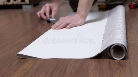 Male Sitting On Floor Cuts Off A Strip Of Wallpaper For Pasting With