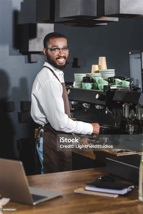커피 자판기에서 커피를 만드는 동안 카메라에 미소 안경에 쾌활 한 젊은 아프리카계 미국인 바리 스타 기업가에 대한 스톡 사진 및 기타 이미지 Istock