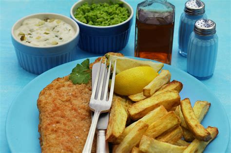 청록색 접시 칼과 포크 레몬 슬라이스 타르타르 소스와 무시 완두콩을 함유한 그릇 식초 병 청록색 배경 전경에 초점을 맞춘 피시 앤 칩스의 클로즈업 이미지 영국에 대한 스톡