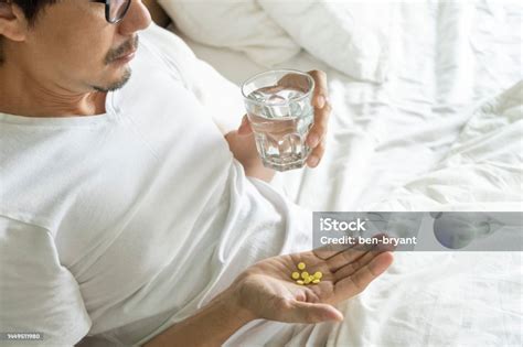 침대에 누워 손에 물과 알약 한 잔을 들고 있는 아픈 아시아 남자를 닫습니다 45 49세에 대한 스톡 사진 및 기타 이미지 45 49세 건강관리와 의술 건강한 생활