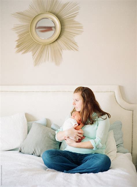 Mother Sitting On The Bed Holding Her Newborn Son By Stocksy