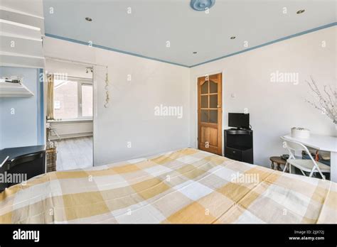 Table Desk With Modern Tv Placed In Light Spacious Bedroom With Blue Ceiling And Bed Stock Photo