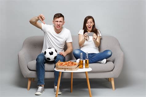 표현 커플 여자 남자 축구 팬은 회색 벽 배경에 고립 된 휴대 전화를 사용 하 여 엄지 손가락을 보여주는 지원 좋아하는 팀을 응원 사람들의 감정 스포츠 가족 레저 라이프