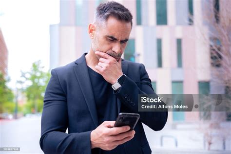 양복을 입은 사려 깊은 남자가 도시 환경에서 야외에서 스마트 폰을 확인하고 있습니다 Brand Name Smart Phone에 대한 스톡 사진 및 기타 이미지 Brand