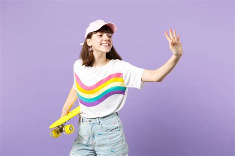 즐거운 십 대 소녀 옆으로 찾고 스케이트 보드 흔들며와 인사와 함께 인사말 보라색 파스텔 배경에 고립 된 사람 사람들은 진심으로 감정 라이프 스타일 개념입니다 복사 공간을