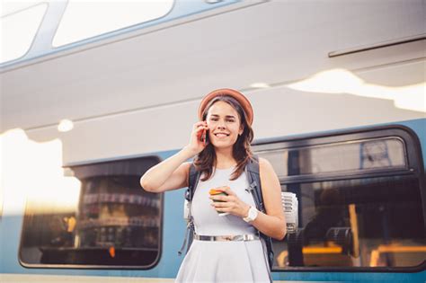 테마 관광 및 여행 젊은 학생 손에 배낭과 컵 커피와 기차 근처 기차역에 서 드레스와 모자에 아름다운 젊은 백인 소녀 스마트폰