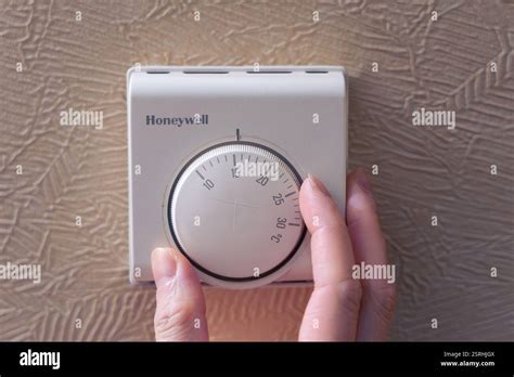 A Woman S Hand Turning A Temperature Dial On A Honeywell Thermostat In