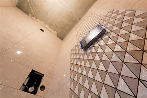 벽에 설치된 가벼운 베이지 색 기하학적 모자이크 세라믹 타일 화장실 및 욕조를위한 장소와 욕실이나 화장실의 미완성 재건 낮은 각도 하단 보기 가정의 방에 대한 스톡 사진 및