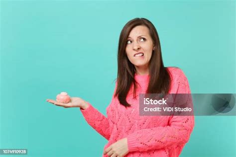 찾고 케이크를 손에 들고와 블루 터키석 벽 배경 스튜디오 초상화에 고립 된 입술을 물고 뜬된 분홍색 스웨터에 젊은 여자 의심 사람들의 라이프 스타일 개념입니다 복사 공간을