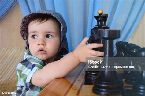 진지한 눈을 가진 모자를 쓴 한 아이가 체스 테이블에 앉아 손으로 말을 들고 있는 모습을 보입니다 체스에 대한 스톡 사진 및 기타 이미지 Istock