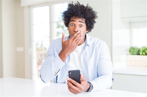 아 프리 칸 아메리칸 남자는 실수로 두려움의 표현 침묵에 무서 워 비밀 개념에 대 한 수치와 충격을 손으로 스마트폰 커버 입을 사용 하 여 가리기에 대한 스톡 사진 및 기타