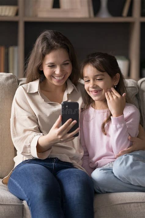 Loving Mom Cuddle With Small Daughter On Sofa Using Smartphone Stock