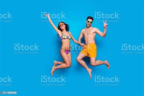 전체 길이 즐거운 젊은 여자와 점프 하 고 손을 안경 수영복을 입은에 행복 한 남자의 초상화 고 파란색 배경에 텍스트 복사 공간 Vsign 공중 부양에 대한 스톡 사진 및