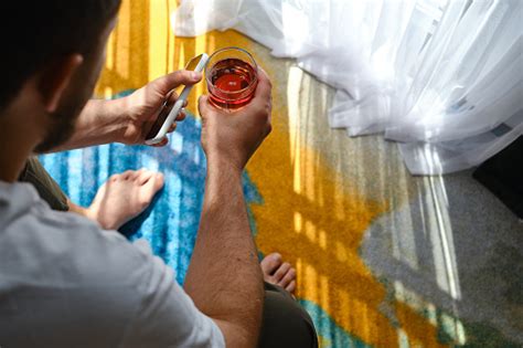 남자는 전화 화면을 보고 술과 함께 마시는 유리를 들고 스카치 브랜디 또는 위스키와 같은 증류주를 맛보습니다 한 남자가 스마트폰을 들고 휴대 전화에 응용 프로그램을