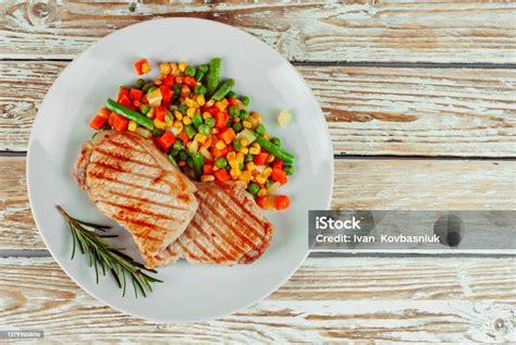 구운 고기 조각 로즈마리와 후추를 화이트 플레이트에 곁들인 스테이크 스테이크 근처의 옥수수 당근 녹색 완두콩 샐러드 플레이트 근처의 텍스트를 위한 공간과 여유 공간을