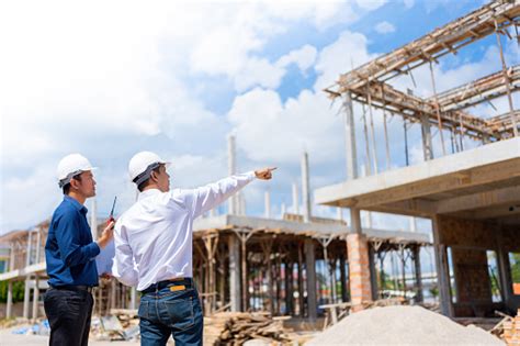 두 명의 엔지니어가 건설 현장 환경에서 함께 작업하고 계획을 세우고 있습니다 건축 사업을 위해 헬멧을 쓰고 손에 라디오를 들고 철골 구조물을 가리켰습니다 2명에 대한 스톡