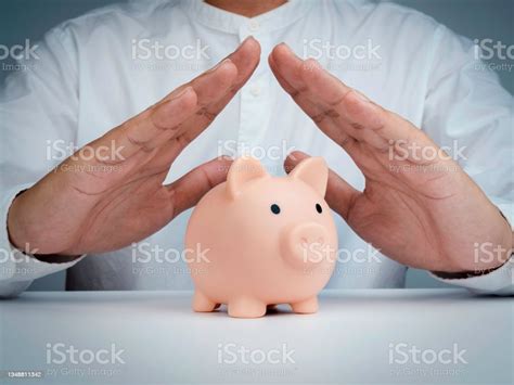 보호 돈 개념 분홍색 돼지 저금통은 흰색 테이블과 어두운 회색 배경에 사업가의 손에 의해 보호됩니다 저축 사업 투자 기금 연금 계획 및 은퇴 개념 가리기에 대한 스톡 사진